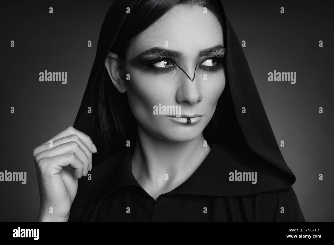 Mysterious witch in mantle with hood on dark background. Black and ...