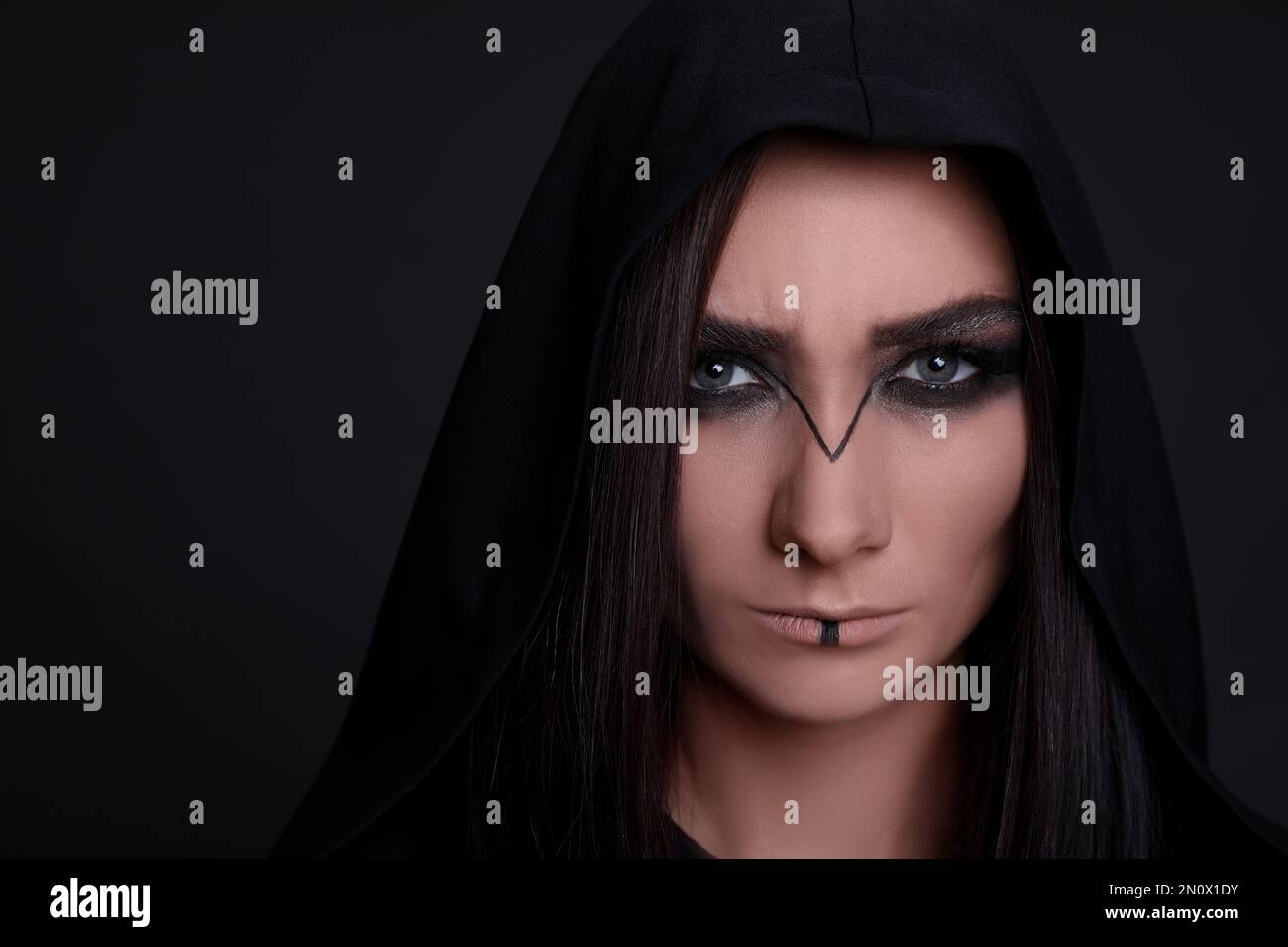 Mysterious witch in mantle with hood on black background, closeup ...
