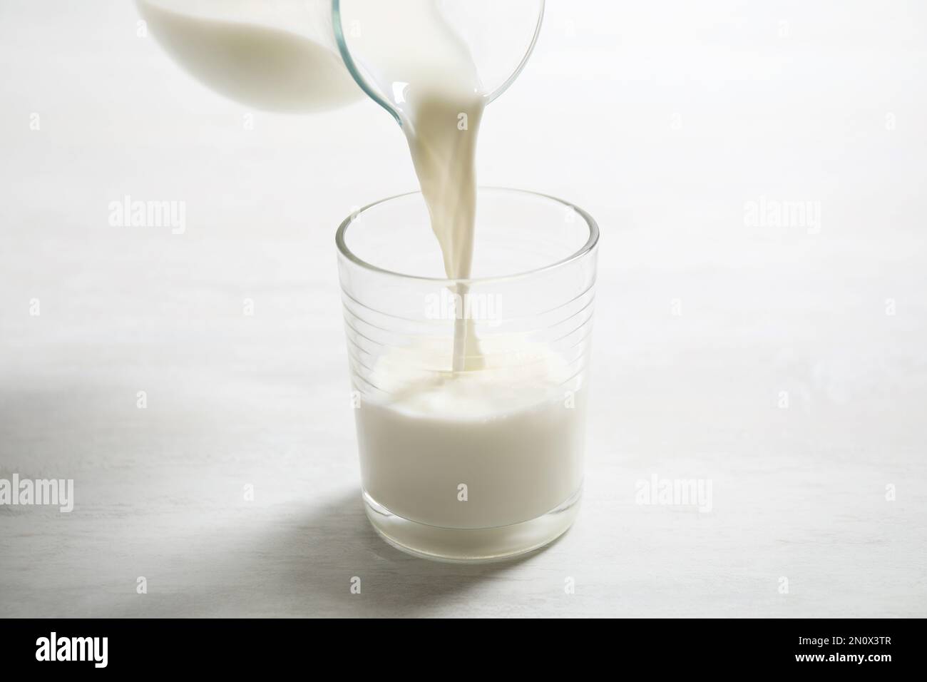 Pouring milk into glass on white table Stock Photo - Alamy