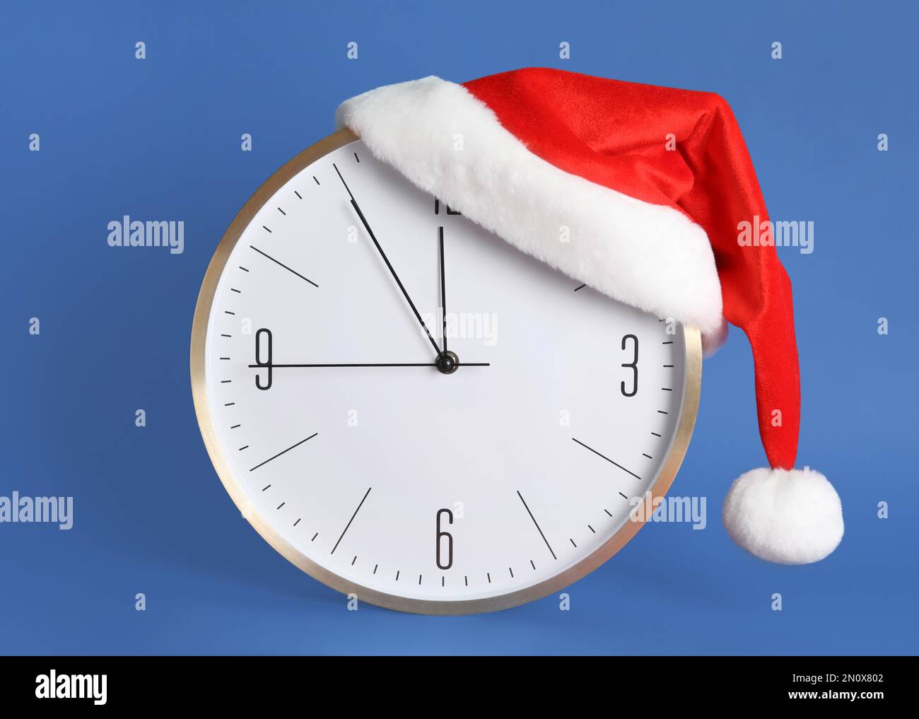 Clock with Santa hat showing five minutes until midnight on blue ...