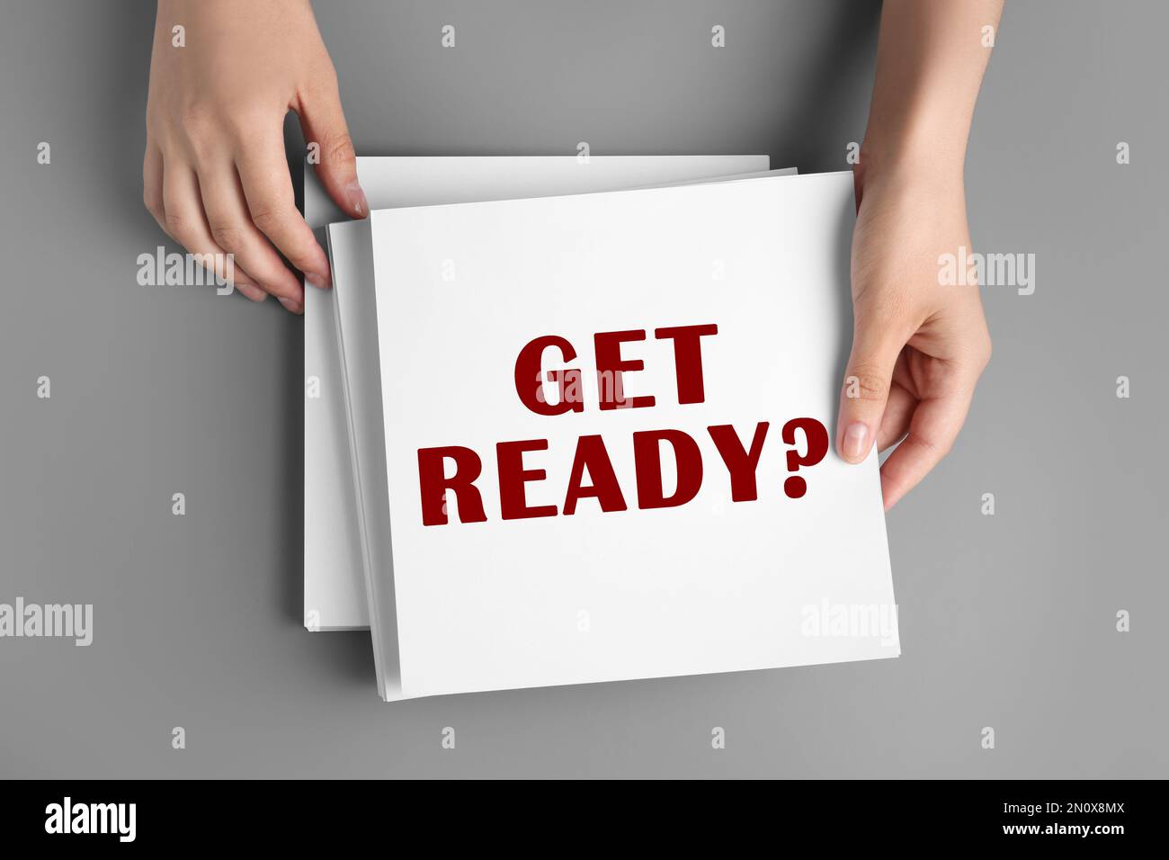 Woman holding paper sheet with text Get Ready? at grey table, top view ...