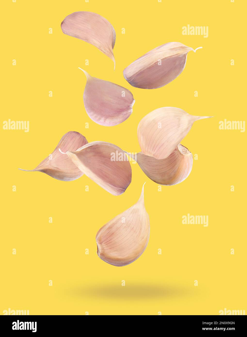 Many garlic cloves falling on yellow background Stock Photo - Alamy