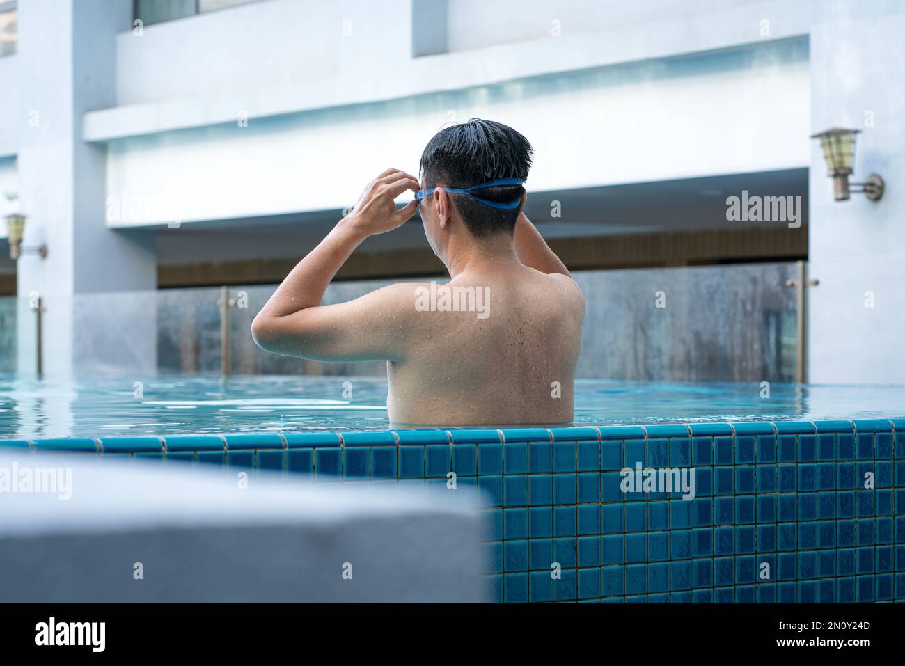 Back view of man in the pool, relaxing and adjusting his goggles by the ...