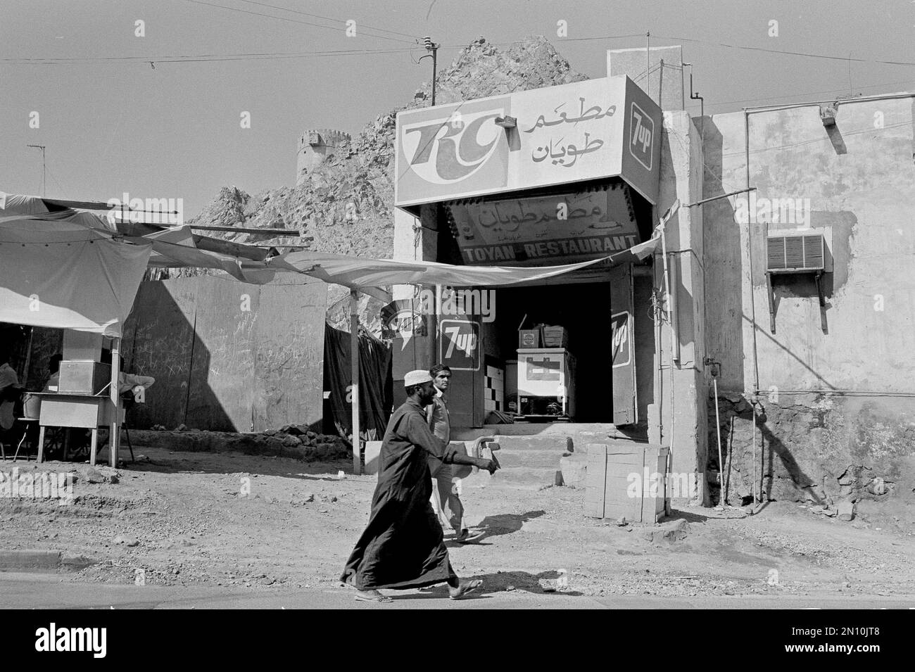 Omani men walk past a restaurant with signs advertising American ...
