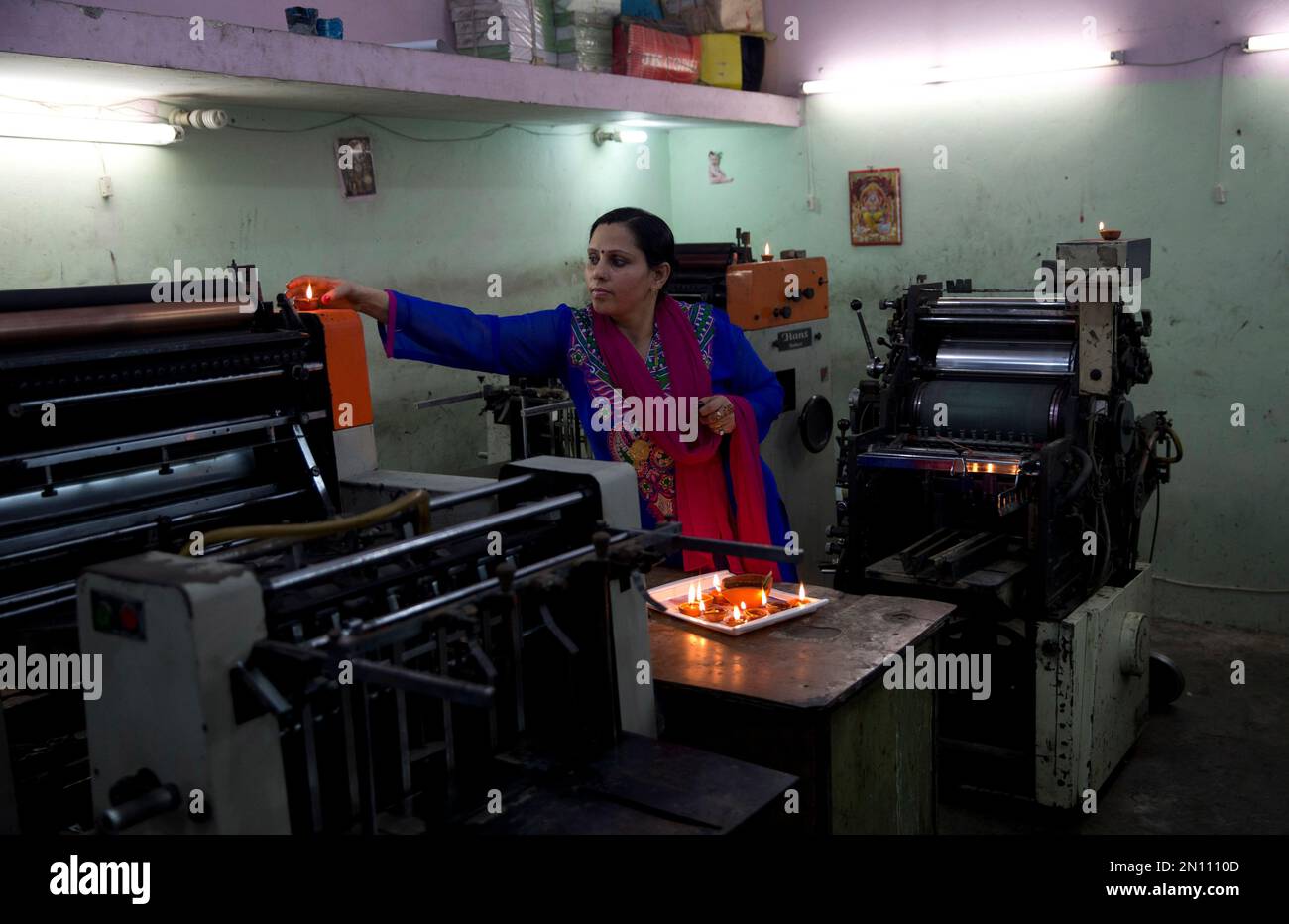 An Indian woman places a lamp on a machine during Diwali in New Delhi ...