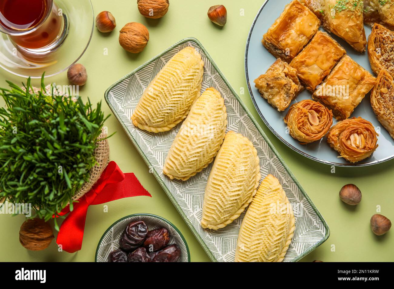 Plates with treats, glass of tea and grass on green background. Novruz ...