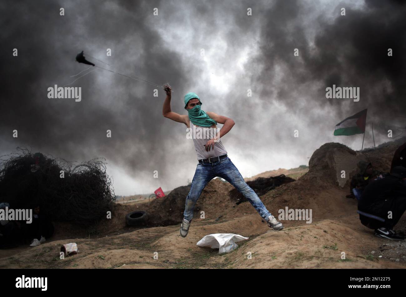 A Palestinian protester hurls stones using a sling shot during clashes ...