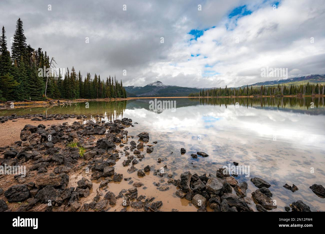 Black stones on the lake shore, landscape with forest reflected in the ...