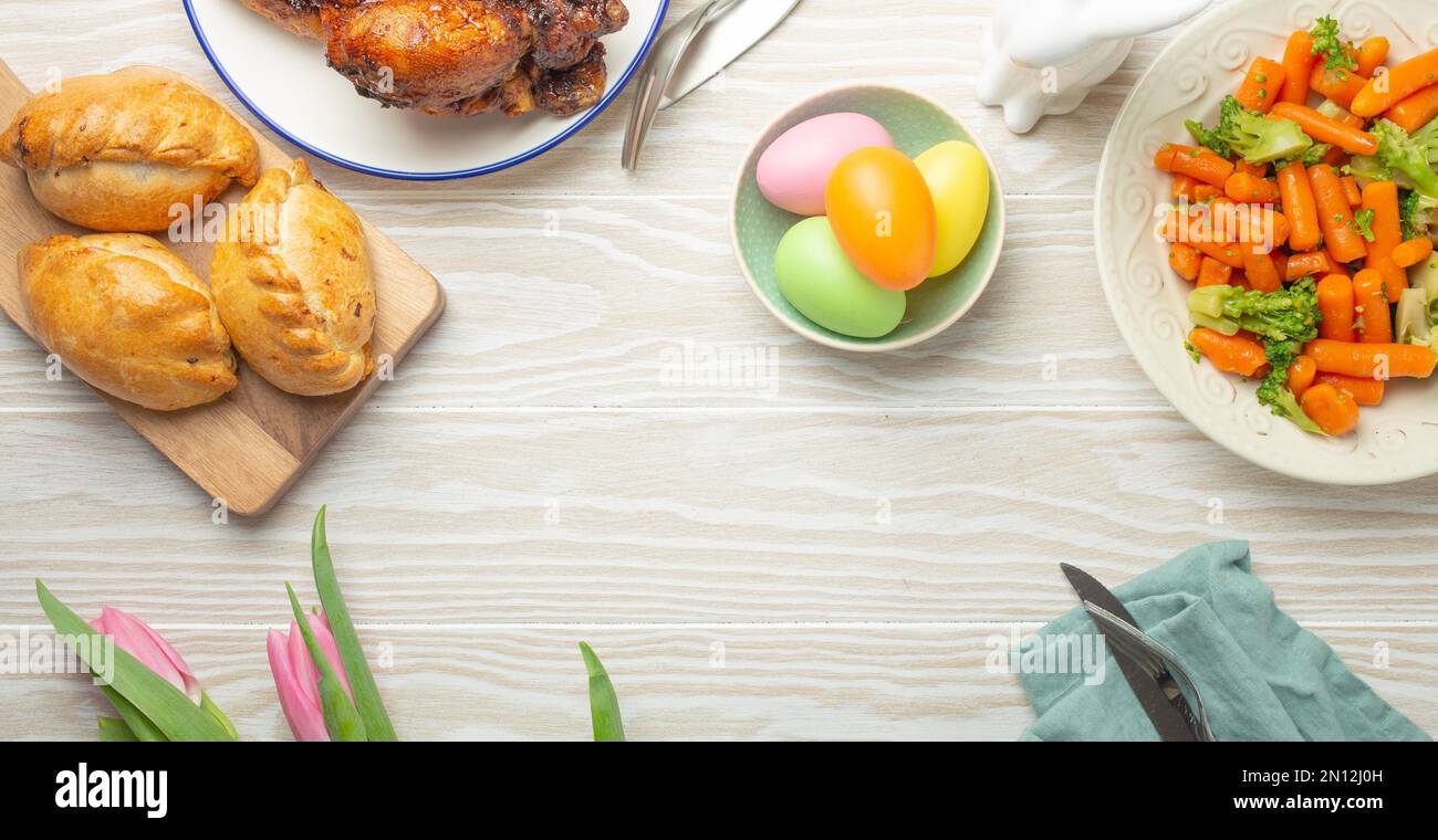 Easter food on white rustic table: pastel colored eggs, roasted chicken ...