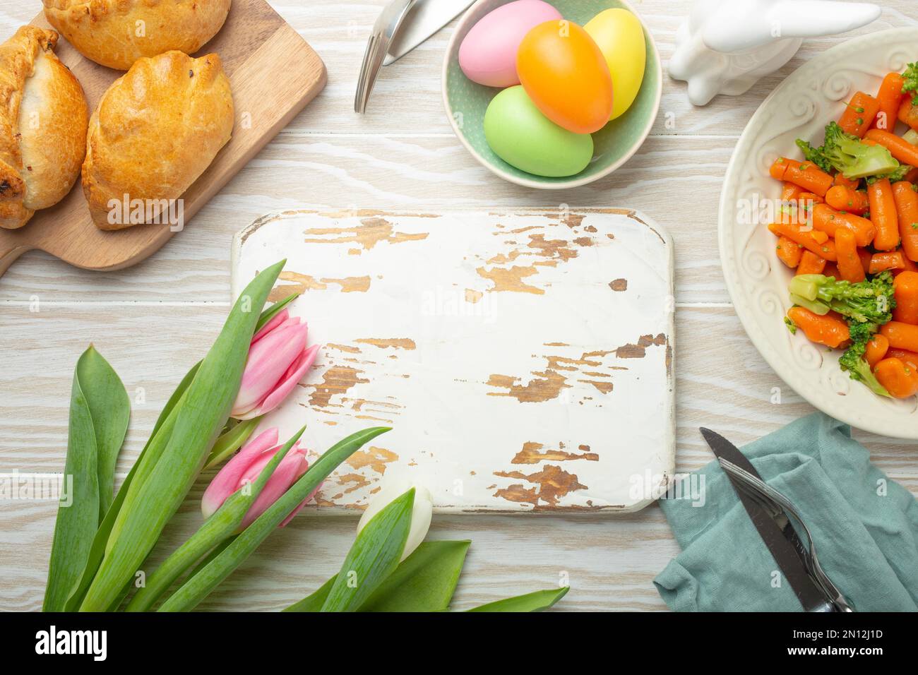 White empty wooden cutting board and Easter food on kitchen table ...