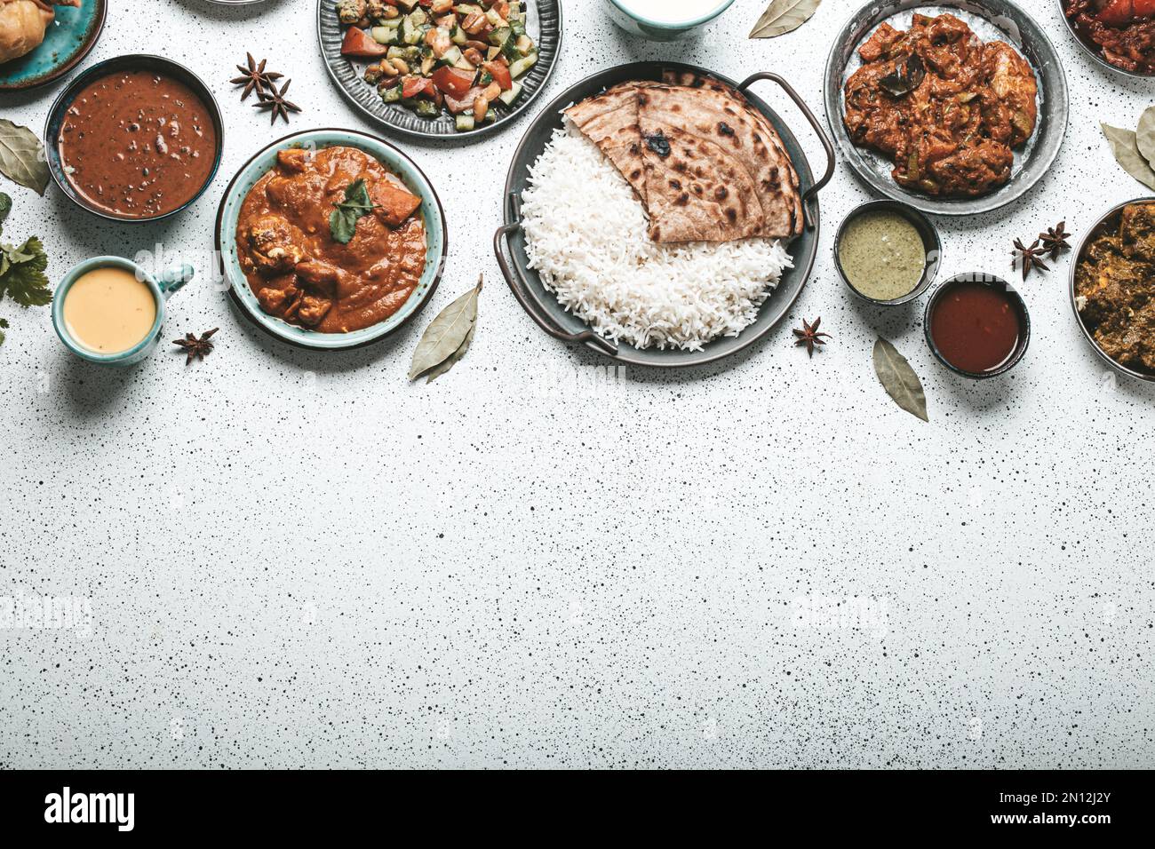 Indian ethnic food buffet on white concrete table top view: curry, samosa, rice biryani, dal ...