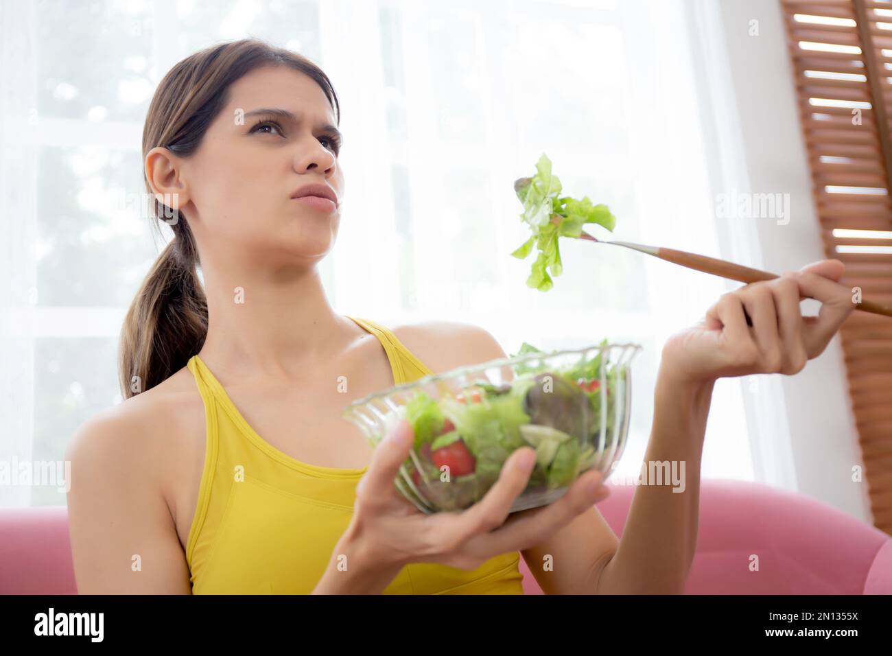Young caucasian woman sitting on sofa eating vegetable salad while ...