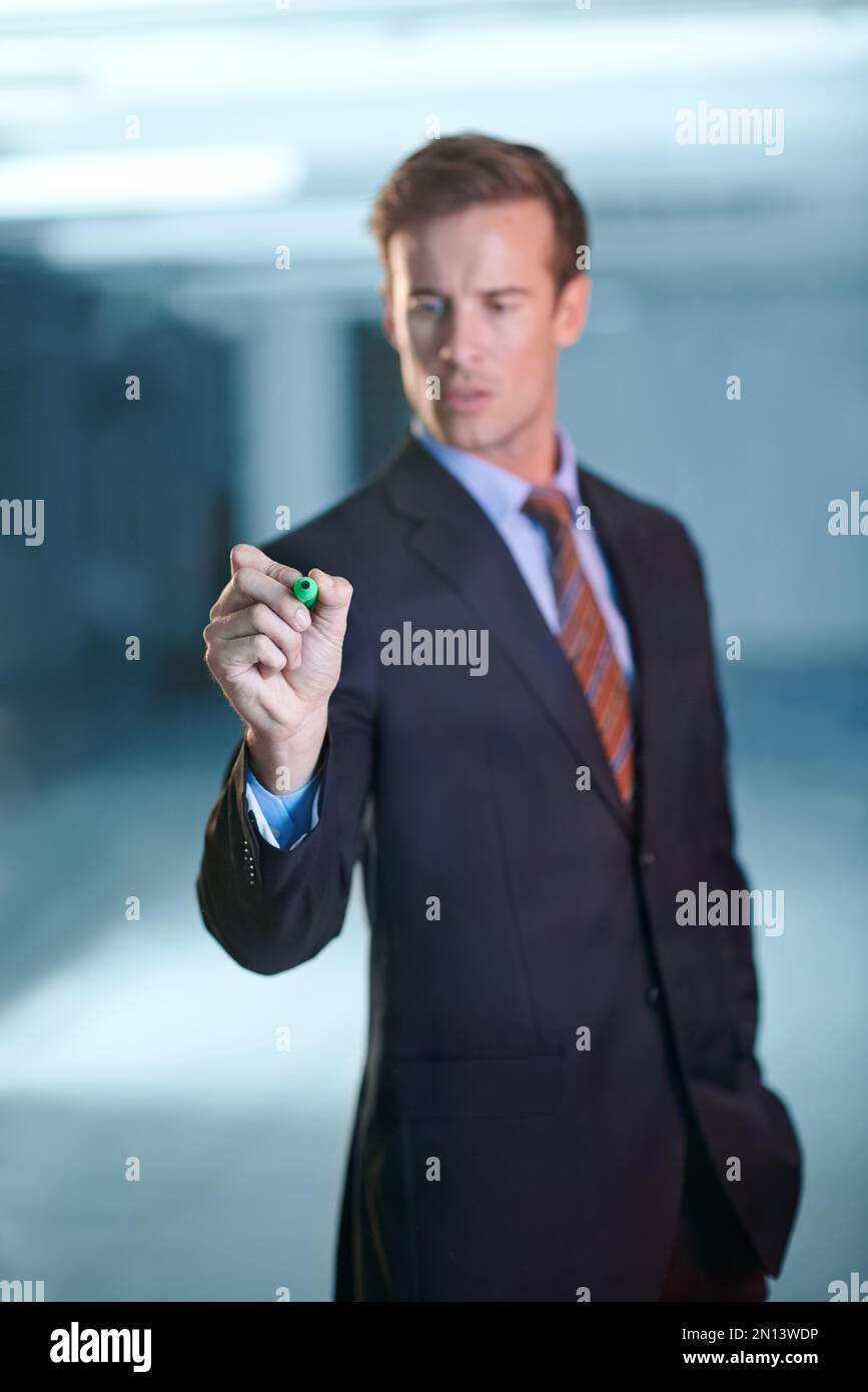Making his mark. a handsome young businessman writing on a transparent surface with a marker ...
