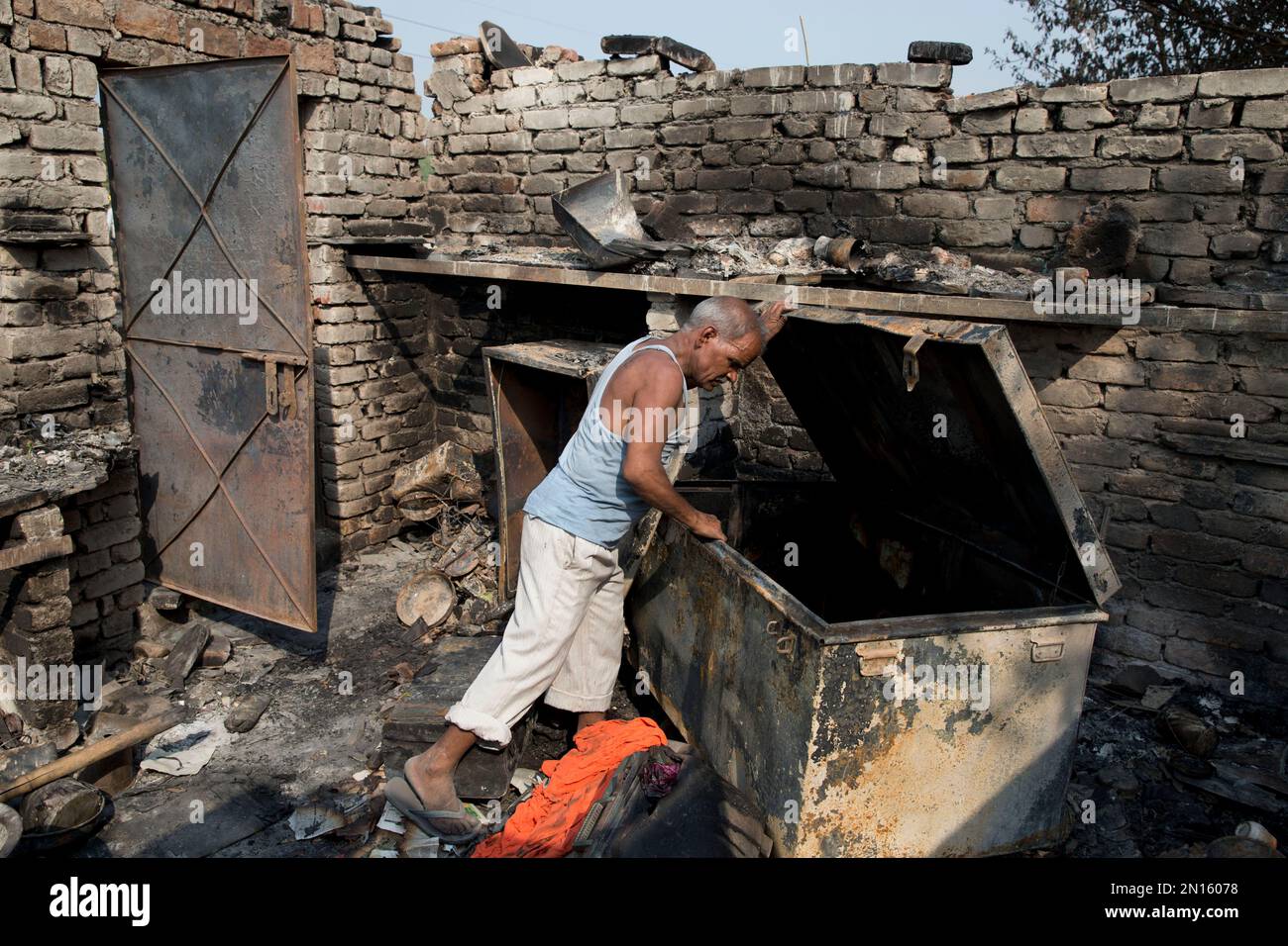 An Indian man looks inside a box at his burned home after a fire broke ...