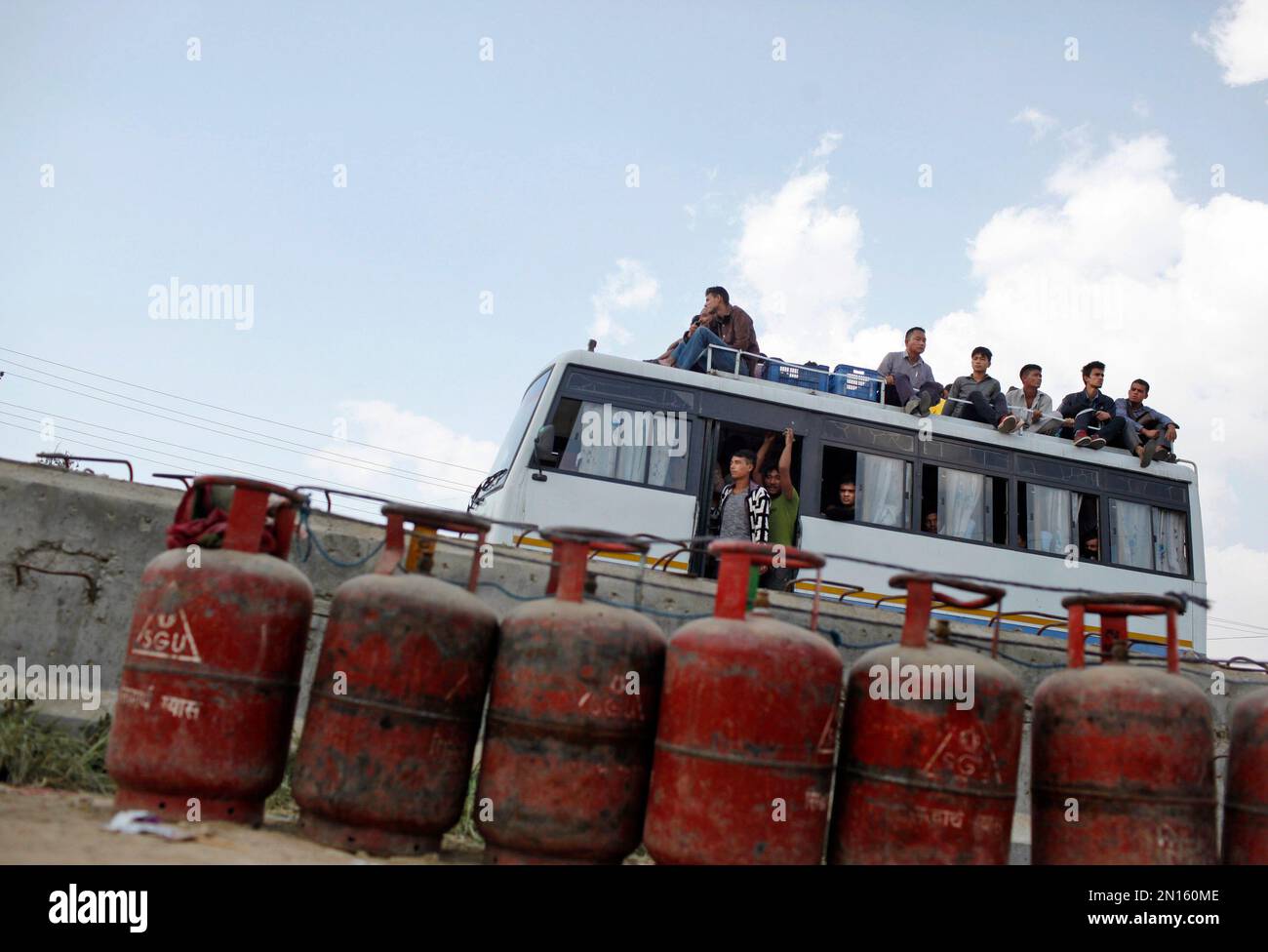 Nepalese people sit on top of a crowded bus as it passes near lined ...