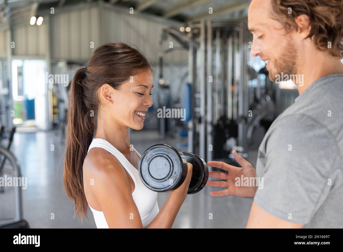 Gym workout personal trainer man helping woman having the right body posture to lift dumbbell ...