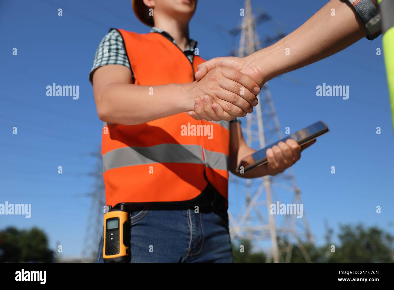 Professional electricians shaking hands near high voltage tower ...