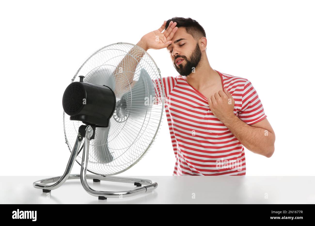 Man suffering from heat in front of fan on white background. Summer ...