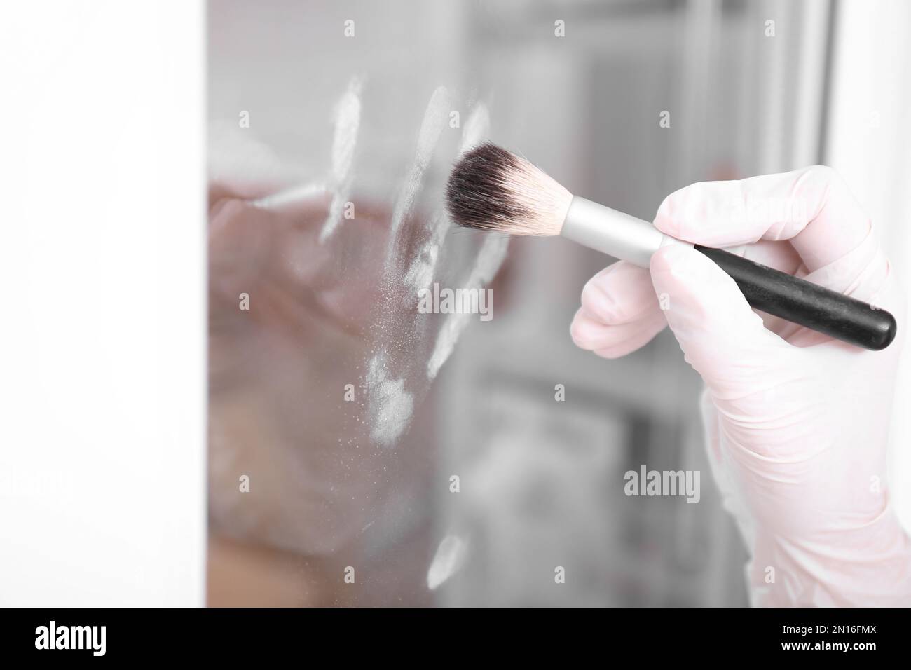 Detective using brush and powder to reveal fingerprints on glass ...