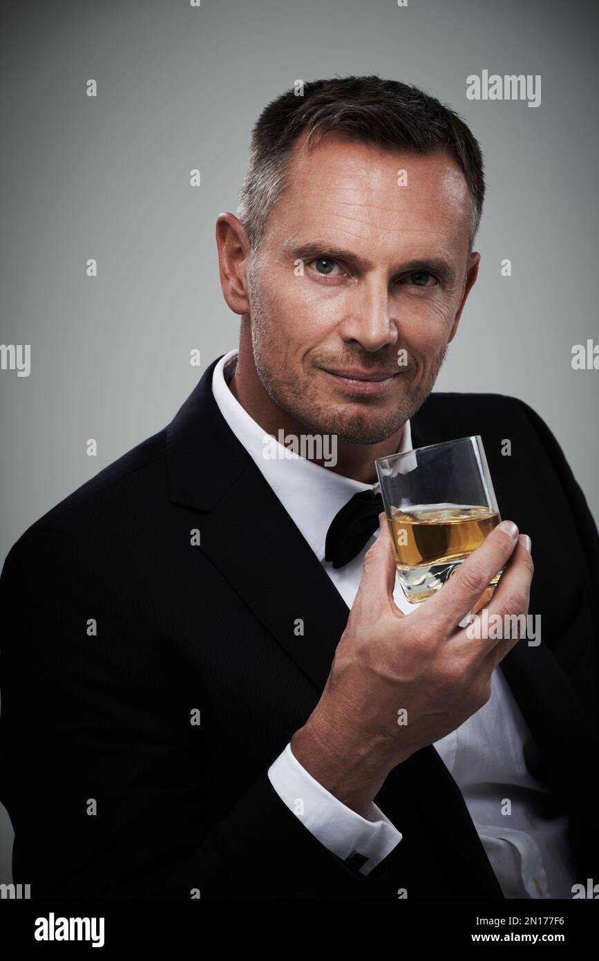 Portrait, whiskey and elegant with a man model in studio on a gray ...