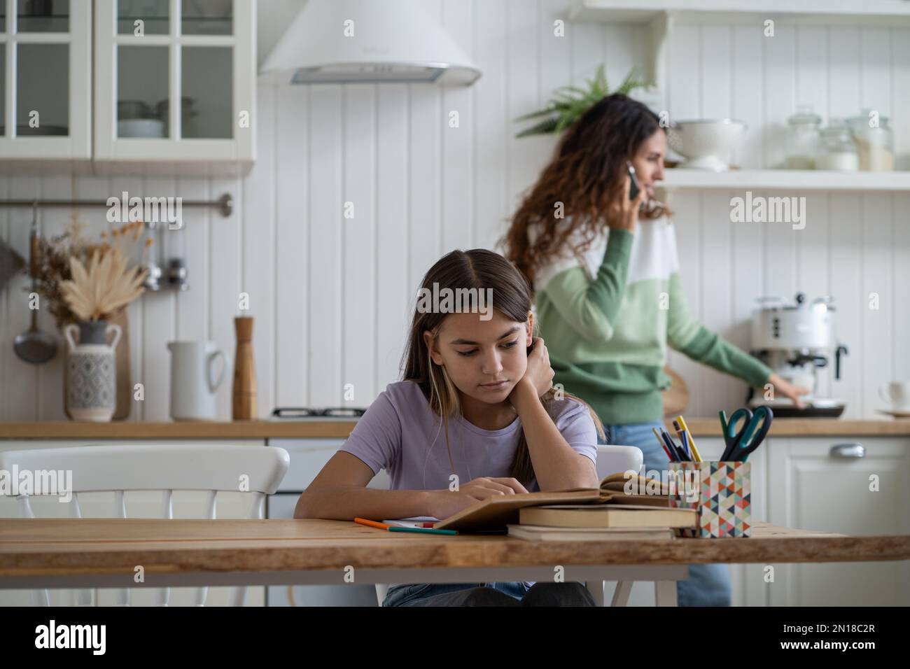 Independent smart teen girl making homework sits at table in dining ...