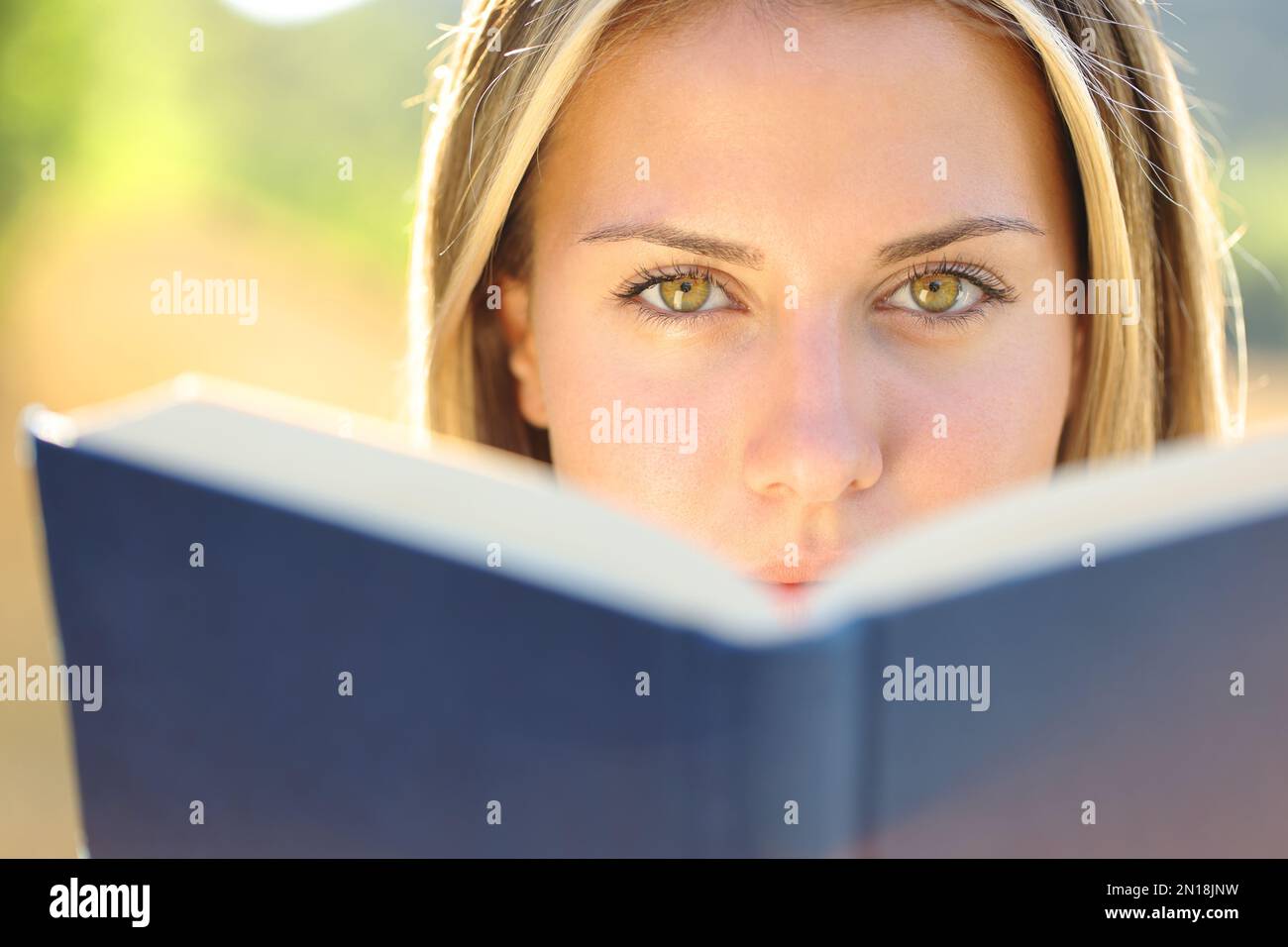 Front view of a beautiful woman reading a book looking at you with ...