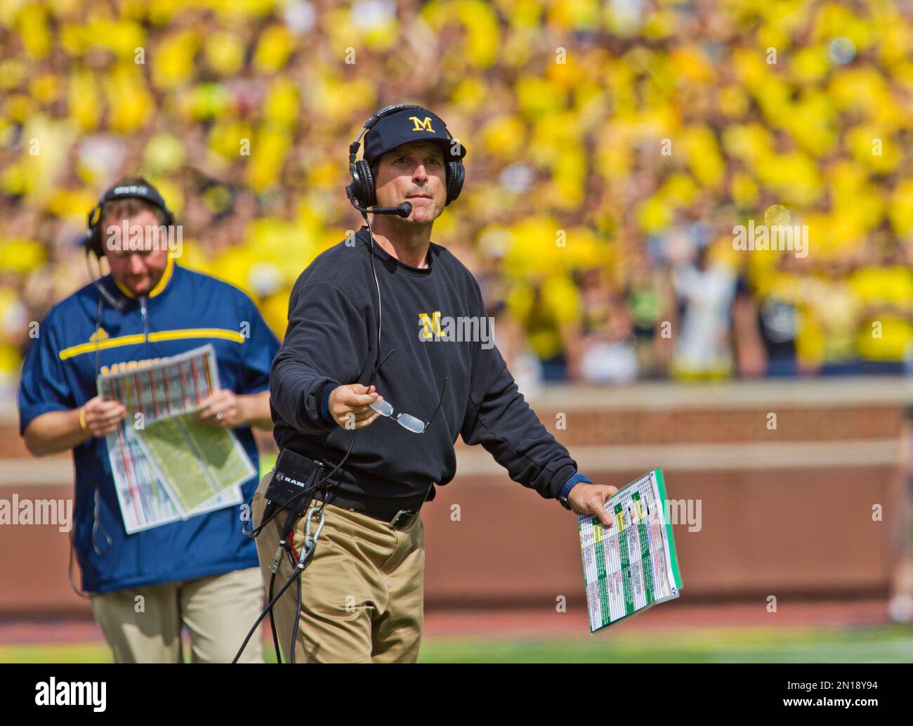 Michigan head coach Jim Harbaugh, wearing a headset and holding on to ...