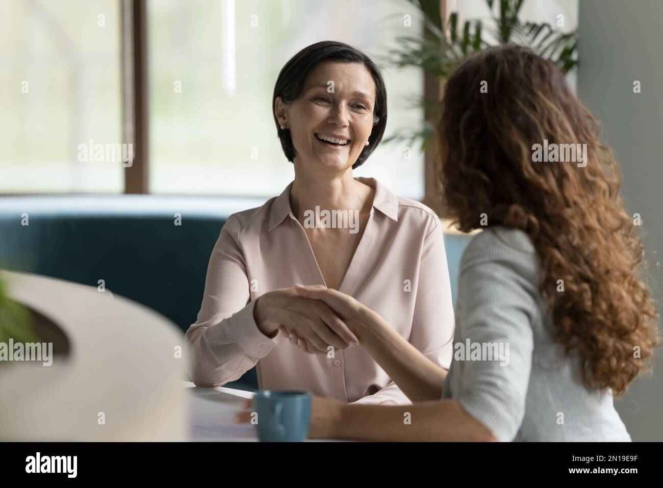 Positive senior business woman giving handshake to younger colleague ...