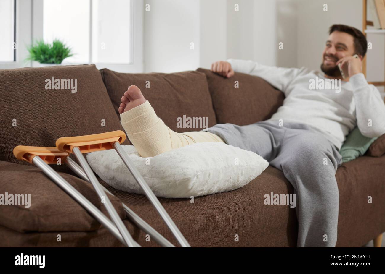 Unhealthy young man with crutches is lying at home on the couch with ...