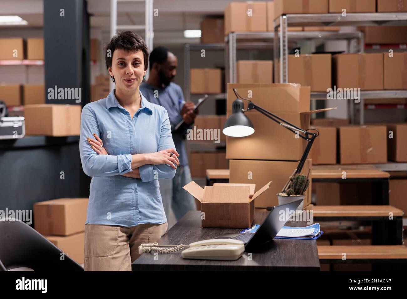Warehouse manager standing in delivery department with arm crossed after finishing packing ...