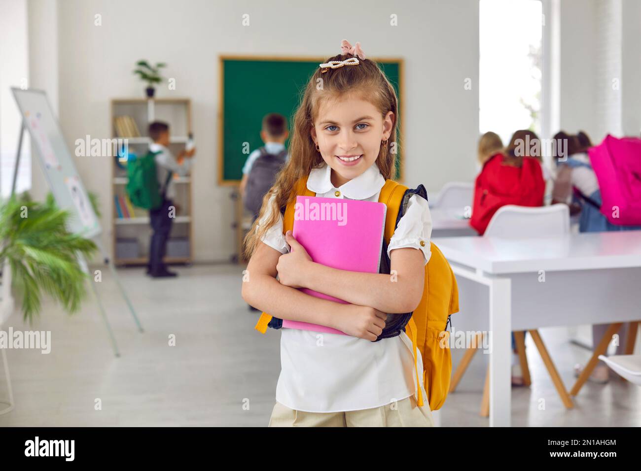 Portrait of happy little elementary school girl posing in classroom ...