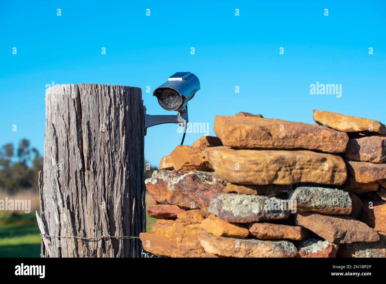 A surveillance security camera attached to a wooden gate post on a farm ...