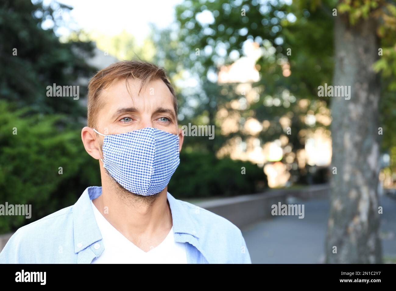 Man wearing handmade cloth mask outdoors, space for text. Personal ...
