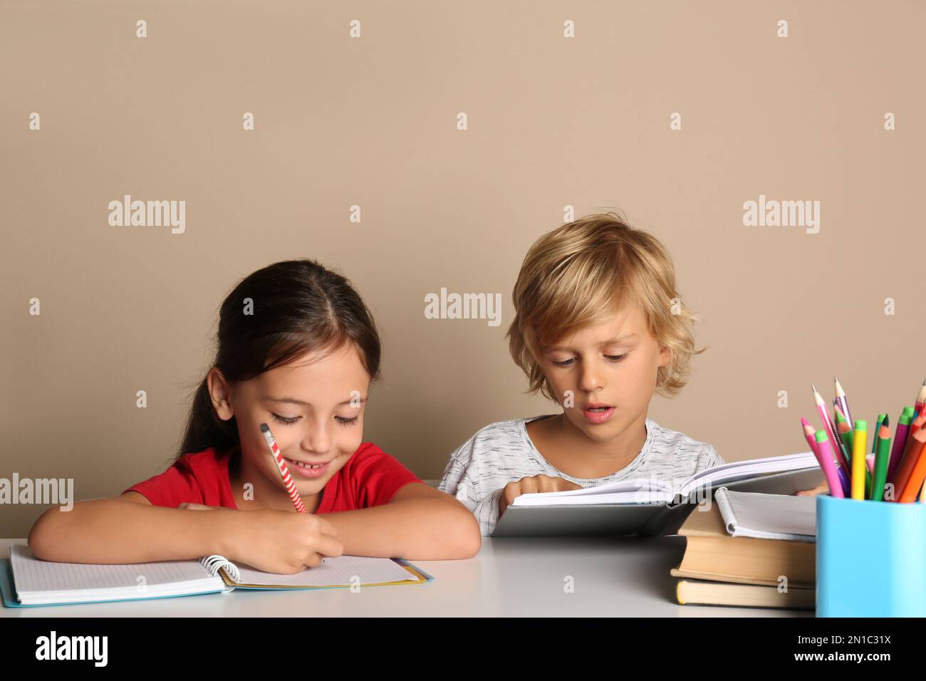 Little boy and girl doing homework at table on beige background Stock ...