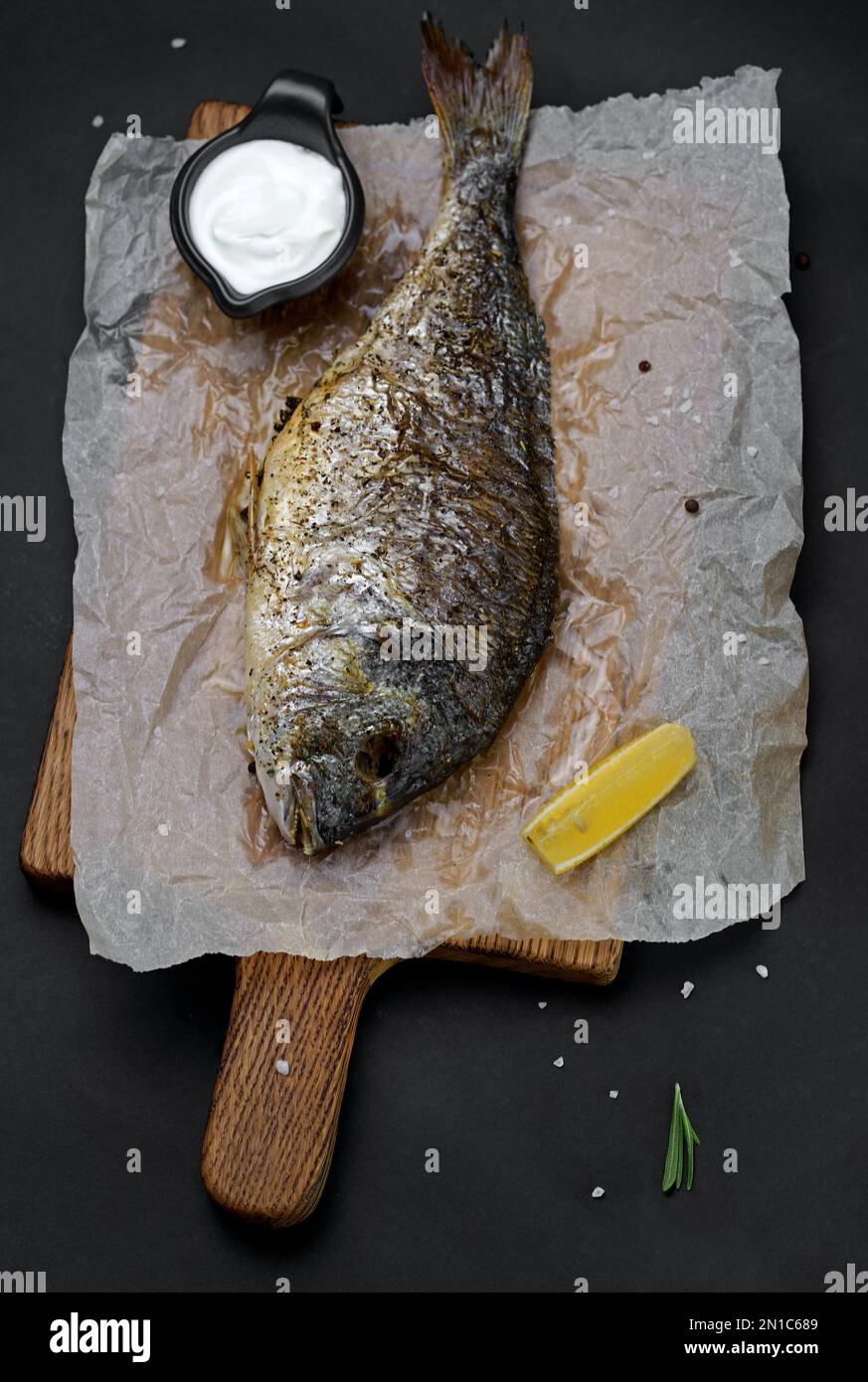 Roasted sea bream fish with herbs on a cutting board. Black background ...