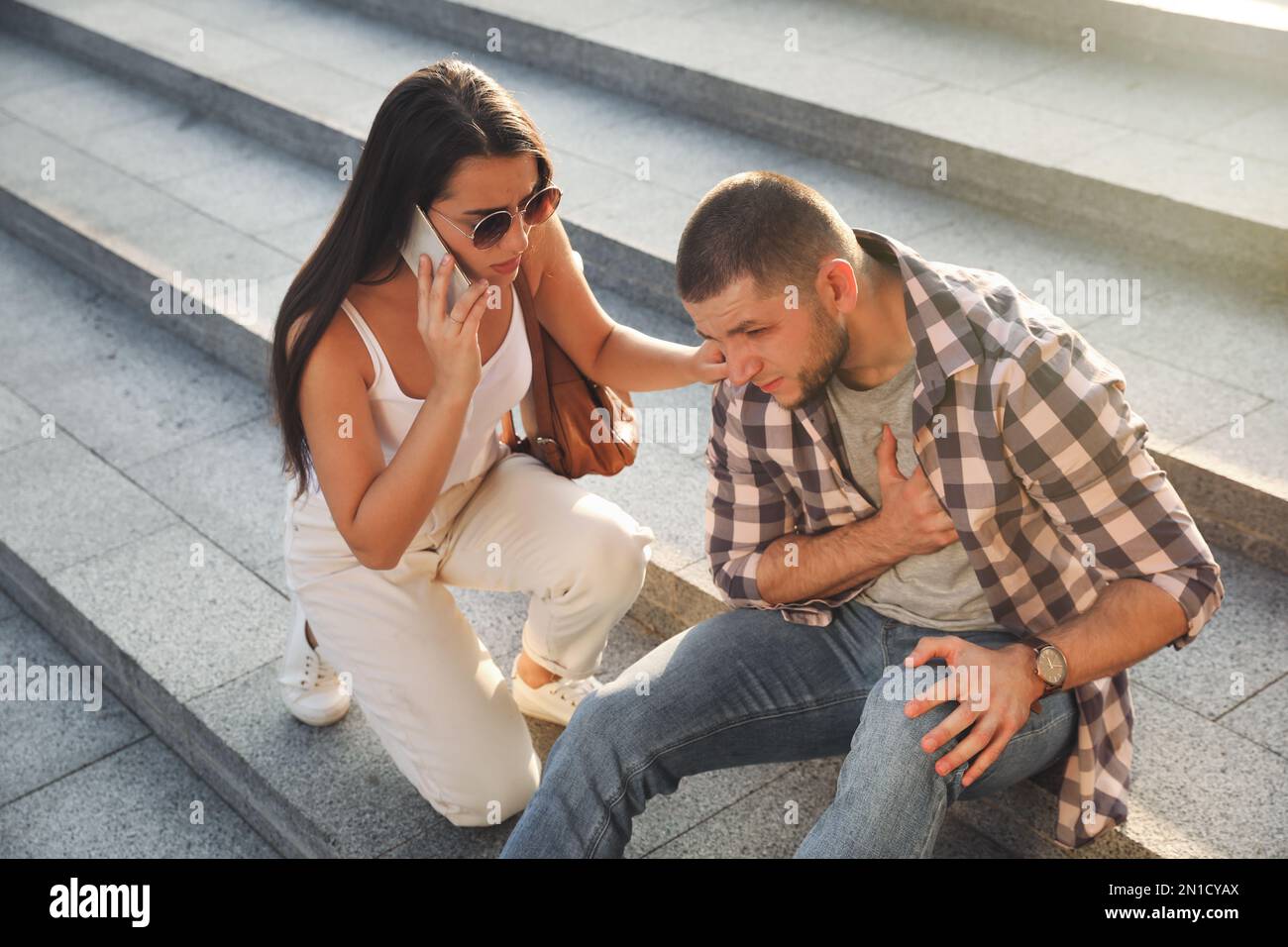 Woman calling ambulance to help man with heart attack on stairs Stock ...