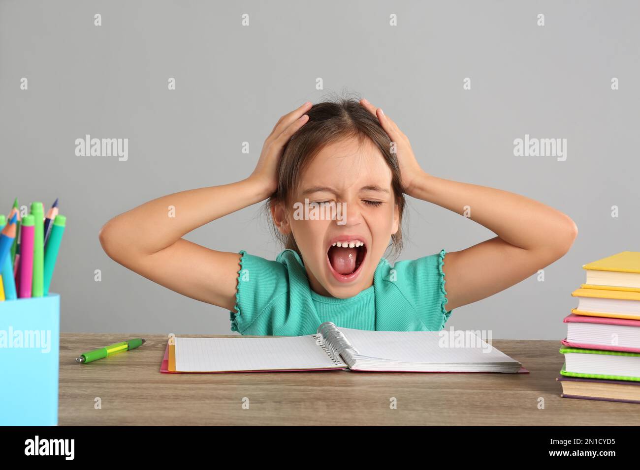 Emotional little girl doing homework at table on grey background Stock ...