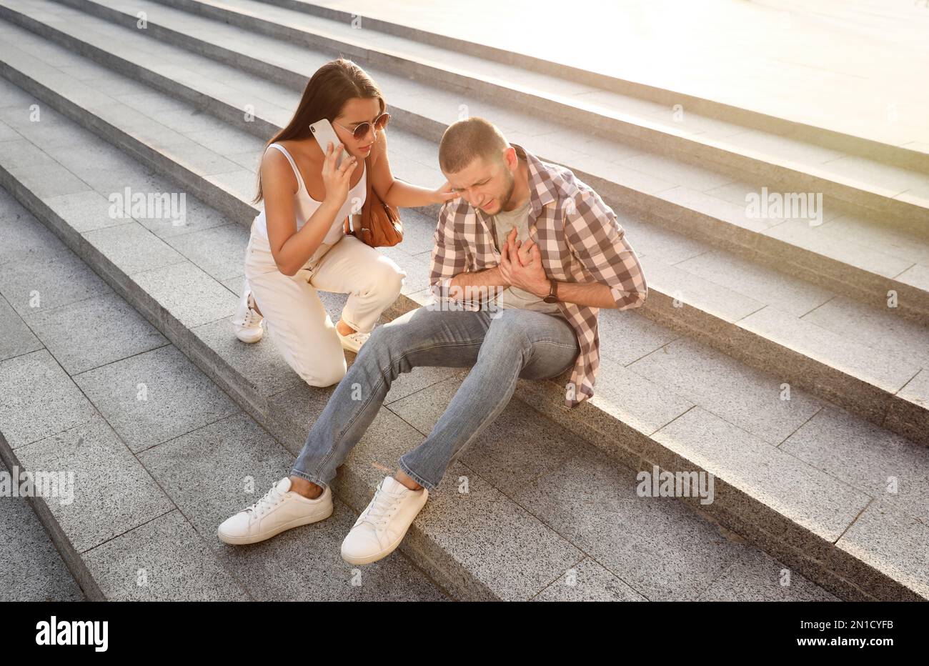 Woman calling ambulance to help man with heart attack on stairs Stock ...