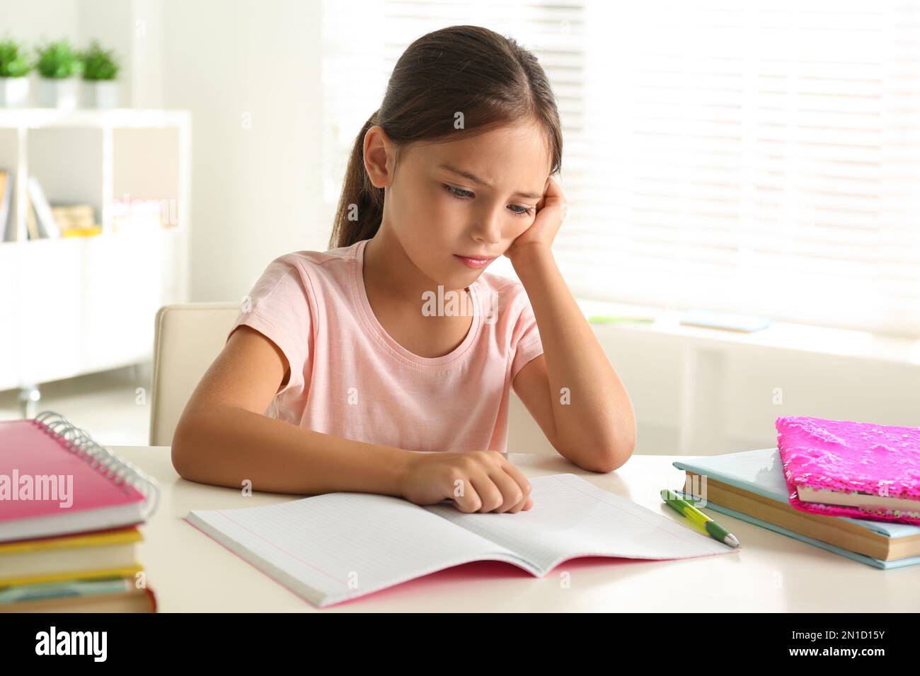 Sad little girl doing homework at table indoors Stock Photo - Alamy