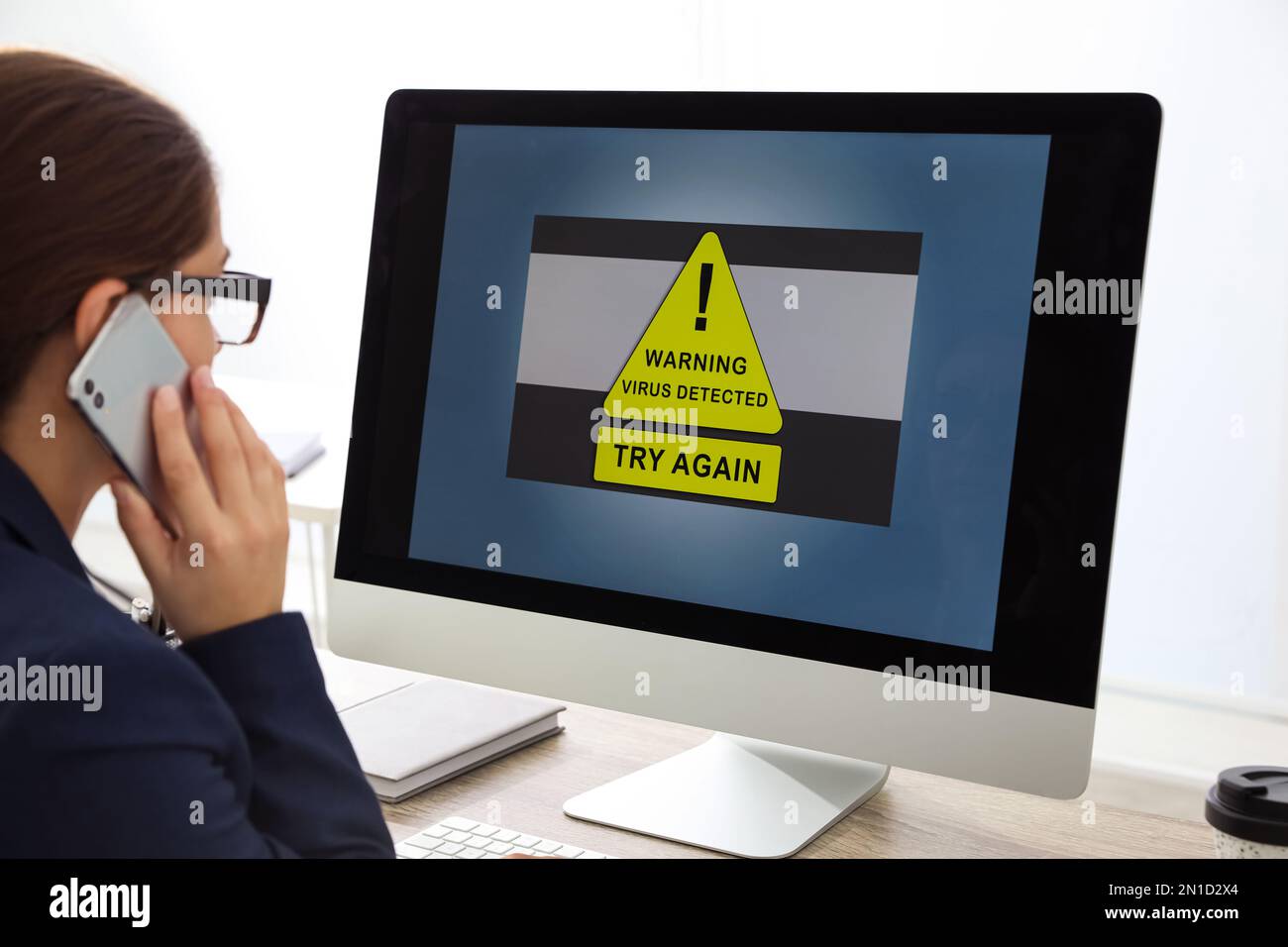Office worker in front of computer with warning about virus attack on ...