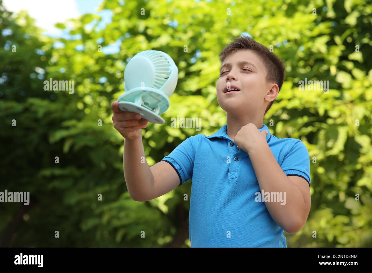 Little boy enjoying air flow from portable fan outdoors. Summer heat ...
