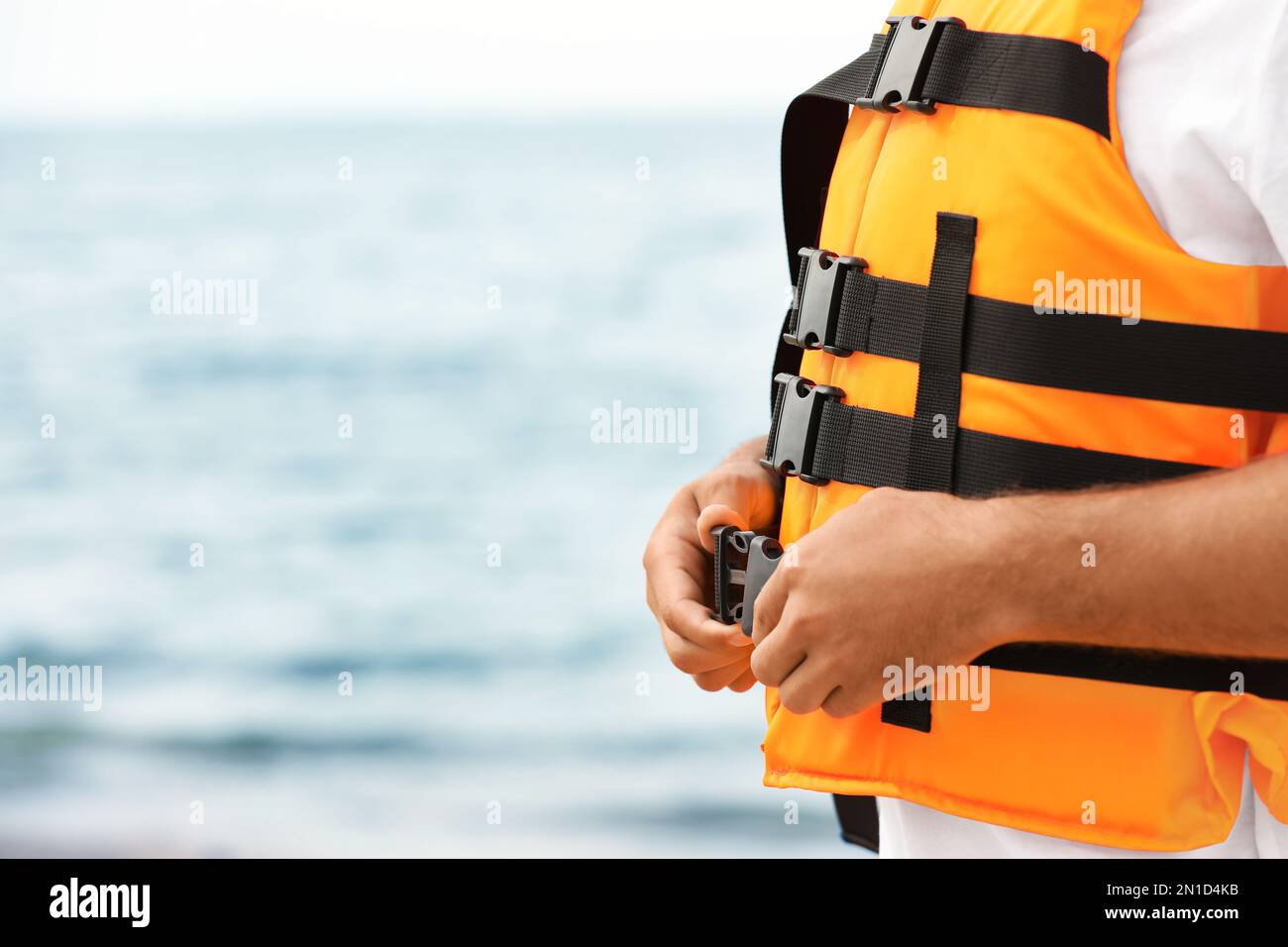 Male lifeguard putting on life vest near sea, closeup Stock Photo - Alamy