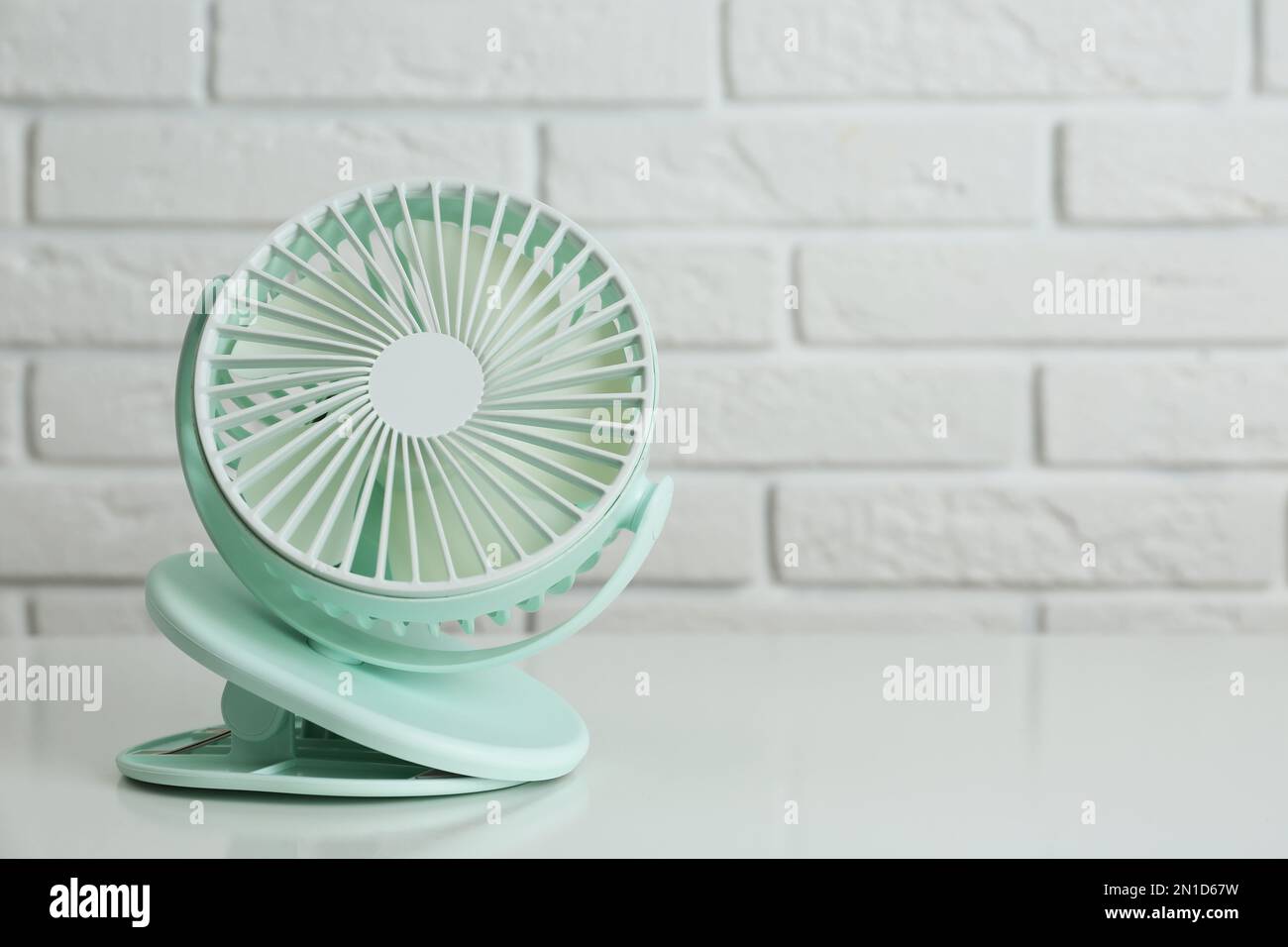 Portable fan on table near white brick wall, space for text. Summer ...