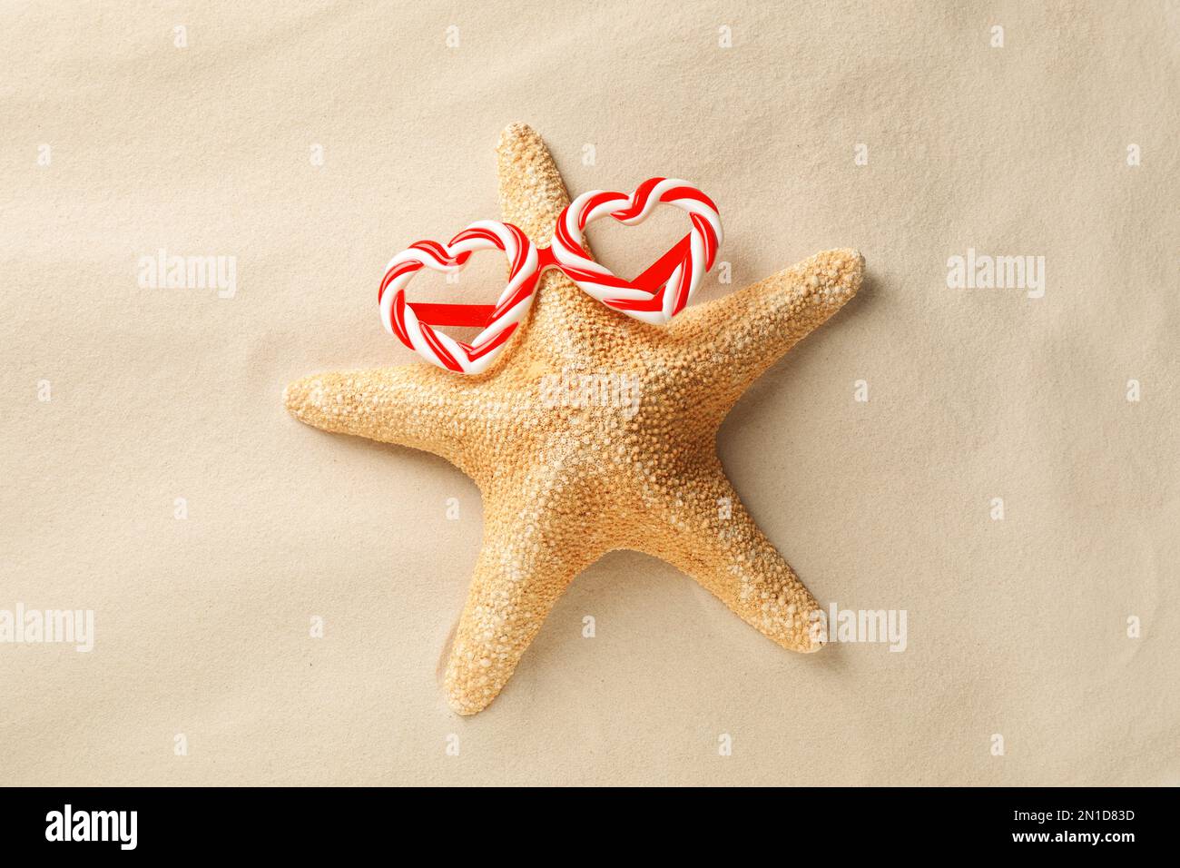 Beautiful starfish with candy cane party sunglasses on sand, top view ...