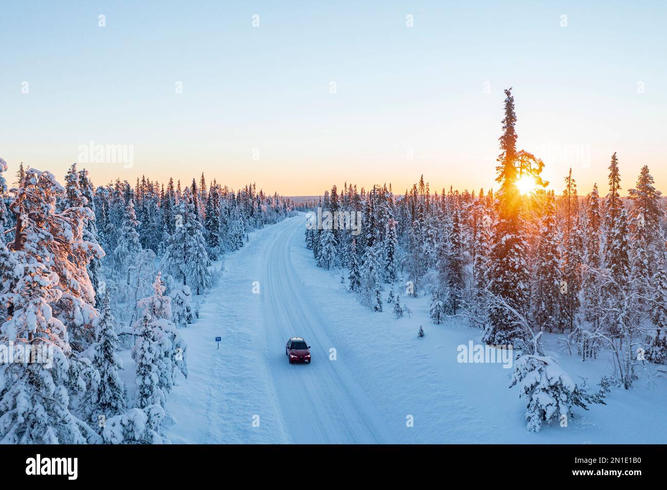 Car traveling on a snowy road in the frozen forest at sunrise, aerial ...