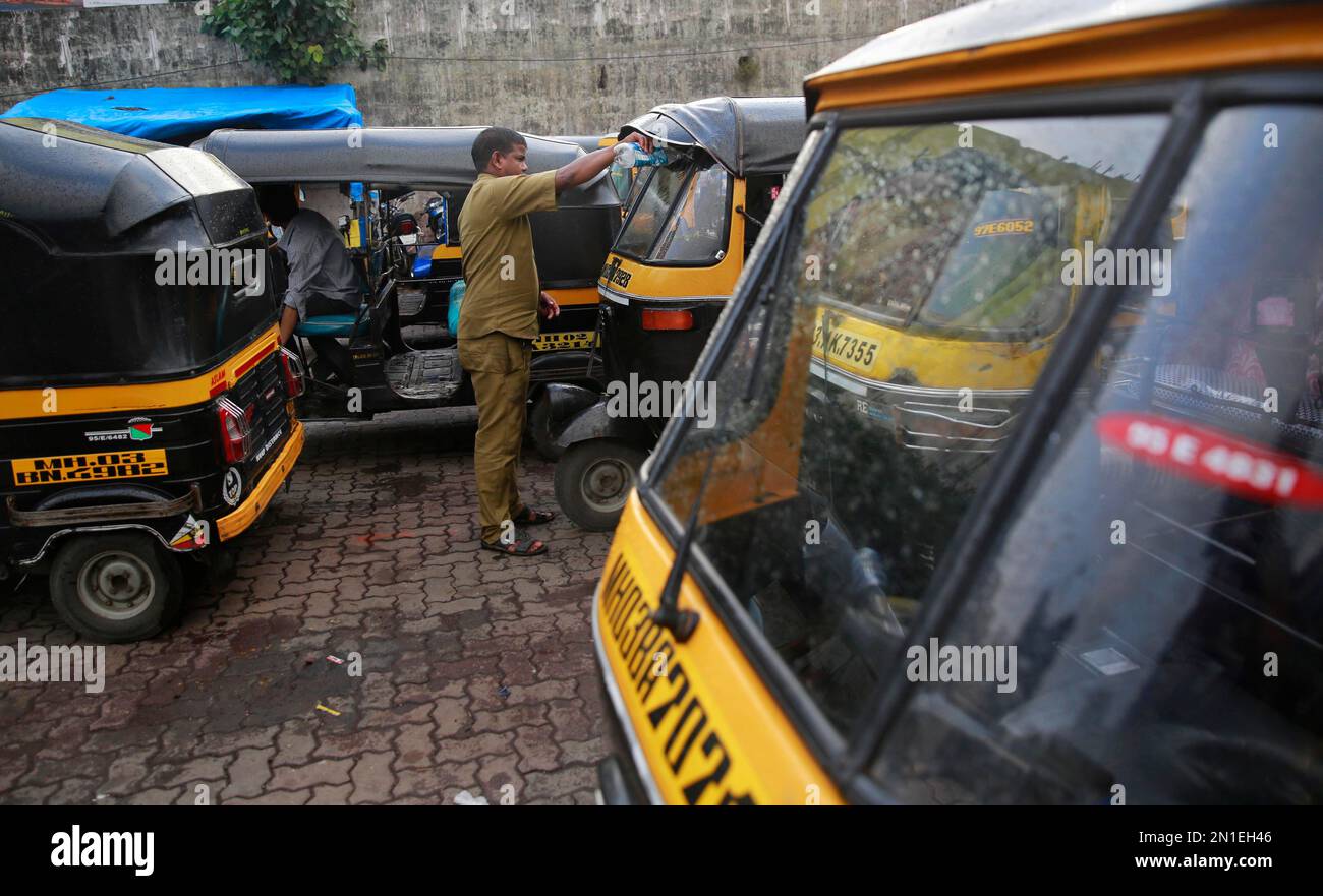 An Indian auto rickshaw driver cleans his vehicle before starting the ...