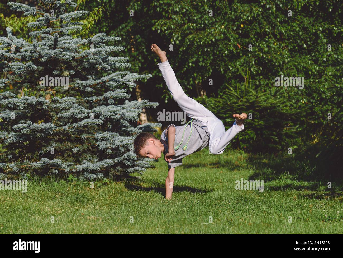 Young caucasian boy playing Capoeira outdoors. Kid exercises acrobatic ...