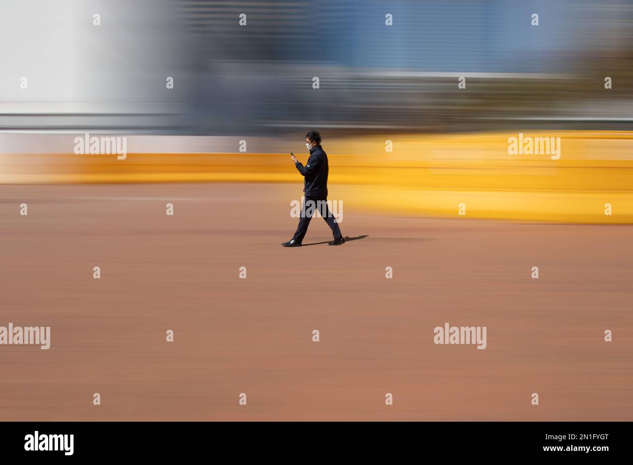 A man walks across an open city space in Hong Kong. Yellow water filled ...