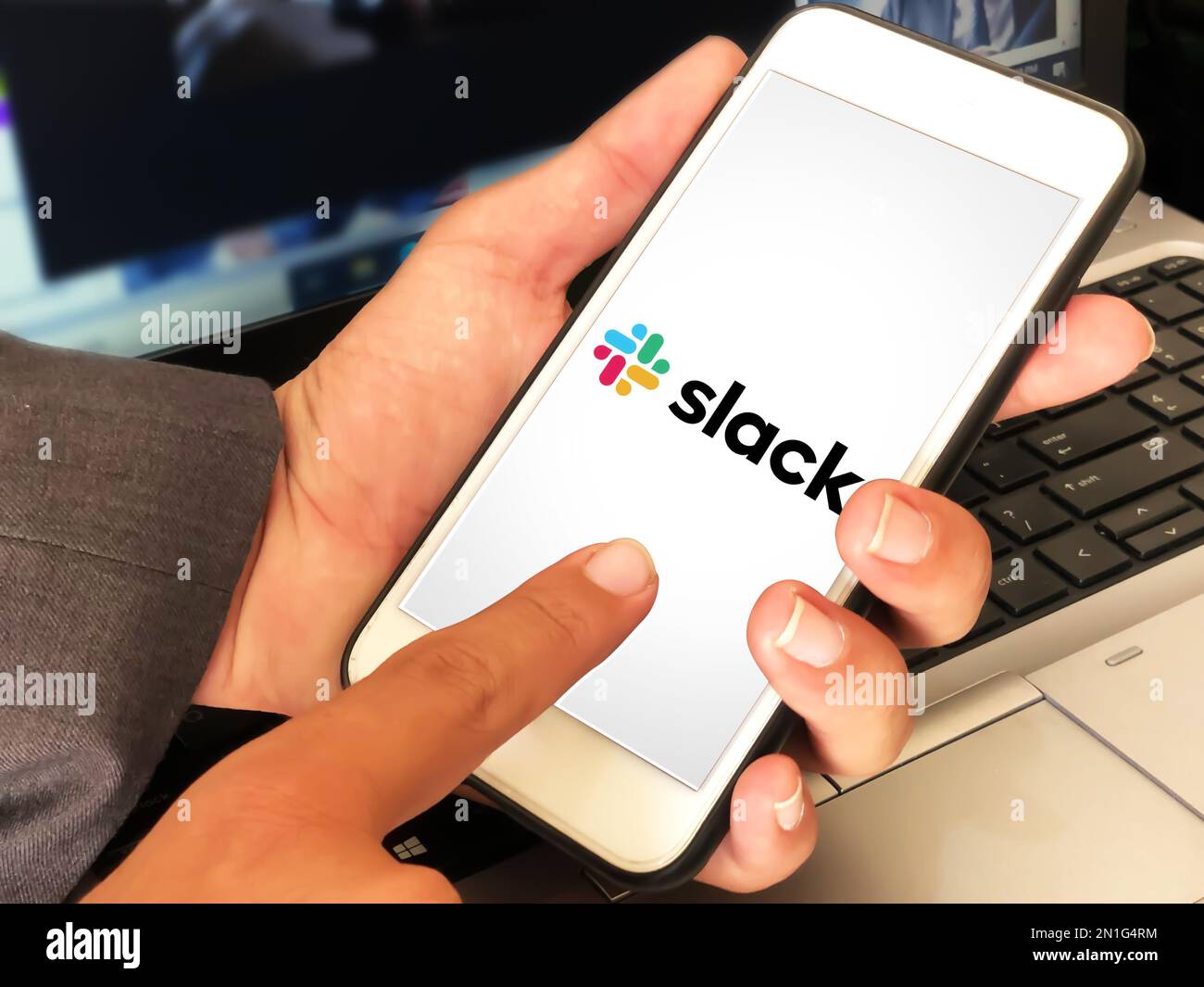 Man using instant messaging platform slack on mobile with laptop screen ...