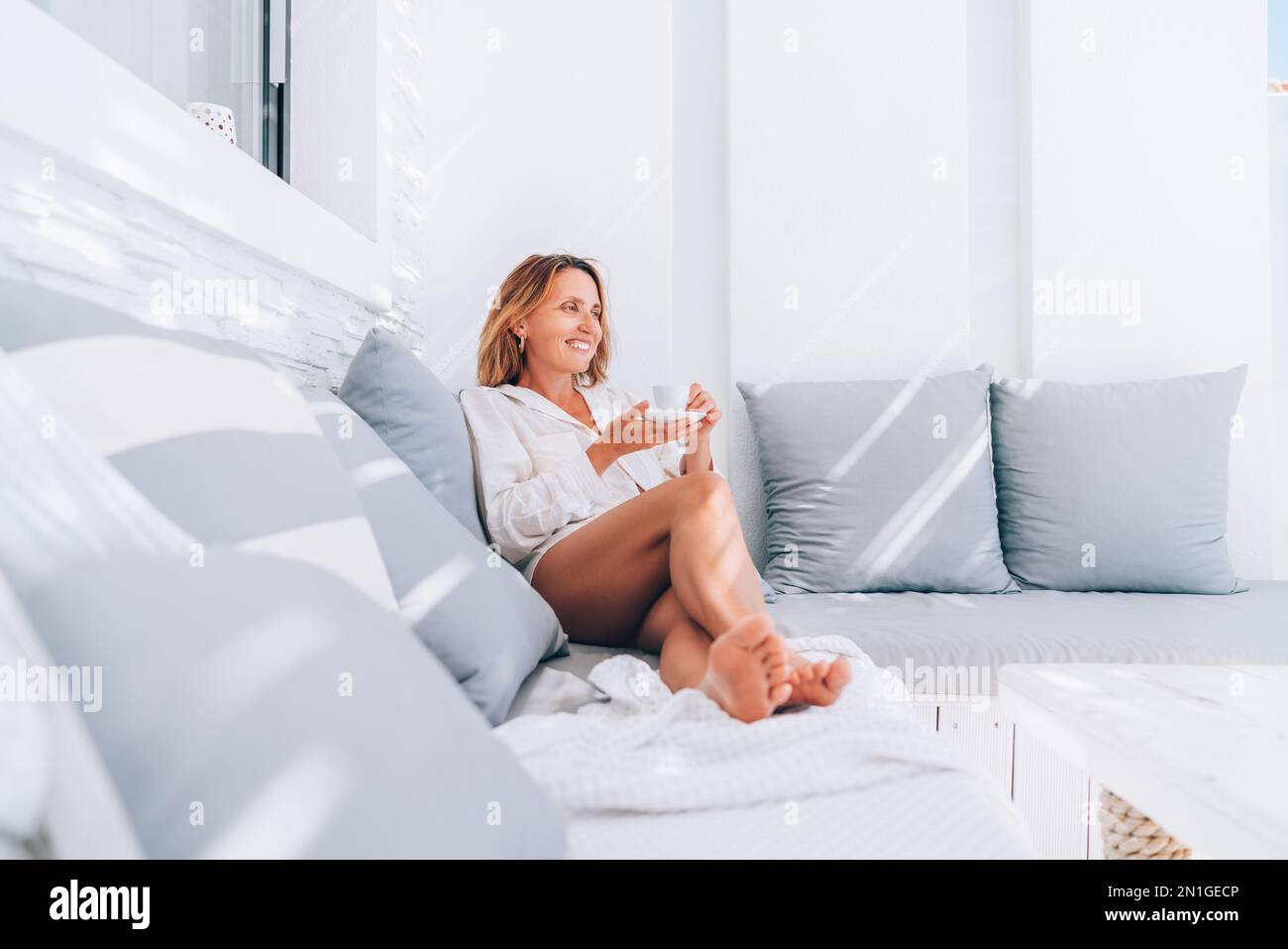 Beautiful barefoot woman dressed white shirt relaxing on luxury terrace ...